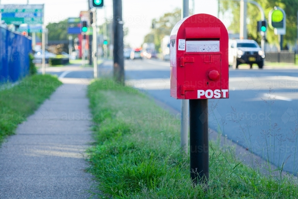 Image of Red post box for mail next to a footpath beside the road ...