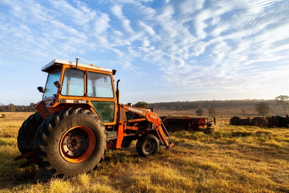 Image of red tractor in a farm paddock in the morning light - Austockphoto