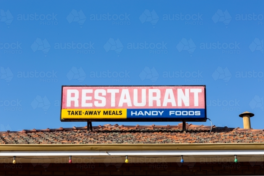 Image of Restaurant sign on tiled roof with blue sky - Austockphoto