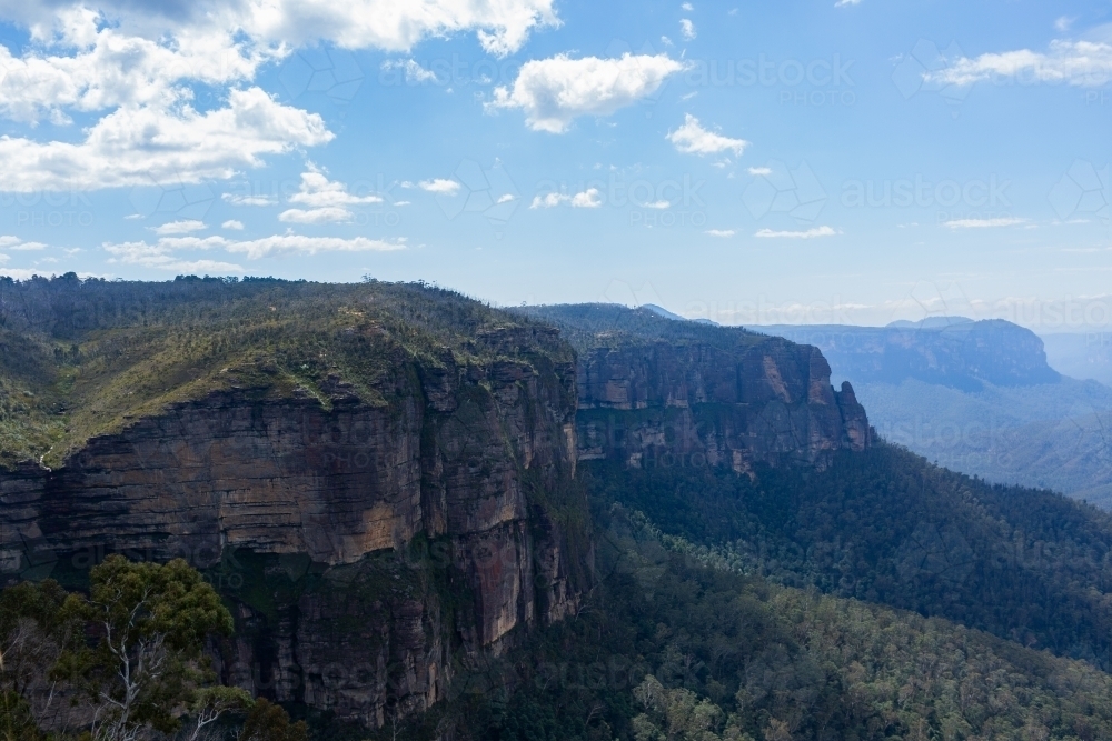Image of Rugged mountain ranges dip into tree filled valley - Austockphoto
