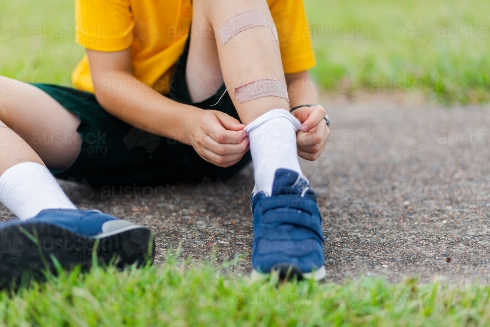 Image of School boy putting on shoes band aids on legs covering scrapes ...