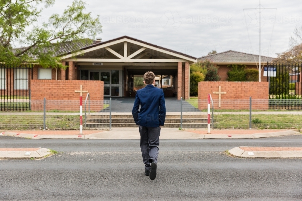 Image of School boy walking across road to school wearing uniform ...
