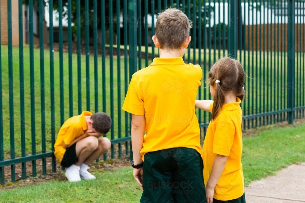 Image of School kids bullying child hunched over by fence - Austockphoto