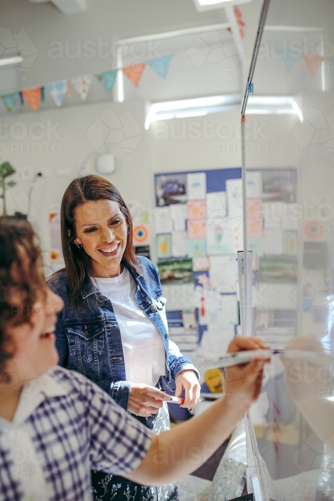 Image of School student writing on a whiteboard with her teacher ...