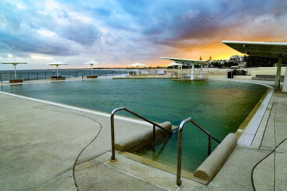 Image of Seaside pool under a dramatic sunset sky. - Austockphoto