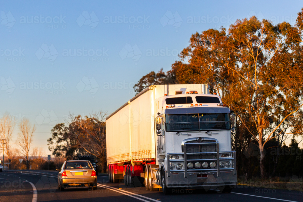 Image of Semi-trailer truck passing car at sunset on country road in ...