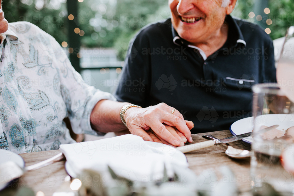 Image of Senior couple holding hands on the table. - Austockphoto
