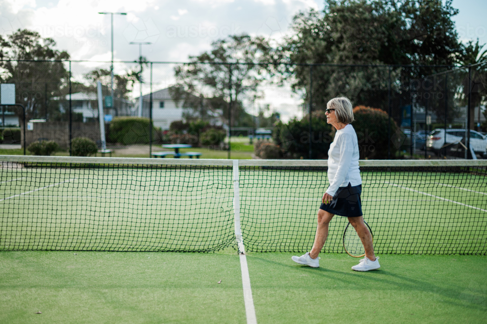 Image of Senior woman in sports attire strolls along the tennis court ...