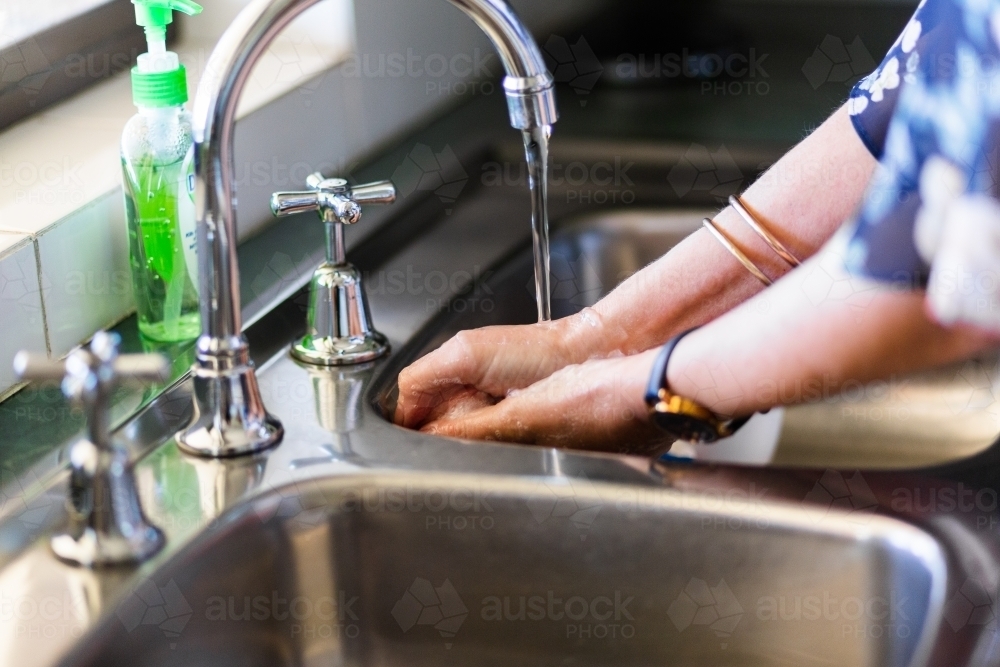 Image of senior woman washing hands with soap in the kitchen sink ...