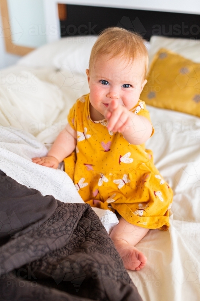 Image of Seven month old baby sitting on parents bed pointing and ...