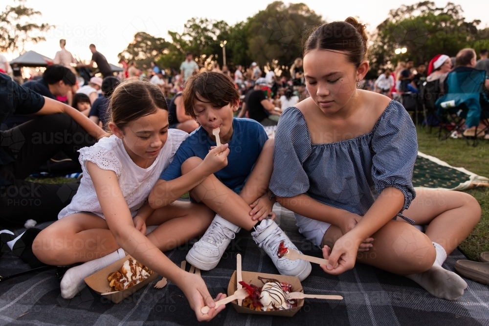 Image of siblings sharing food on a picnic rug in the park - Austockphoto