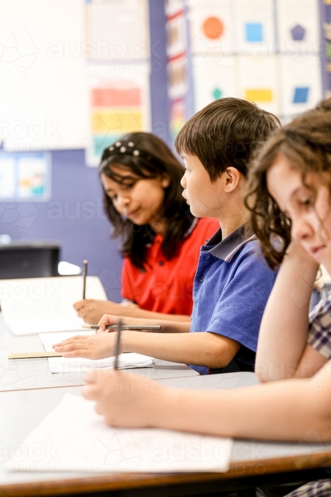 Image of Side view of students writing in the classroom - Austockphoto