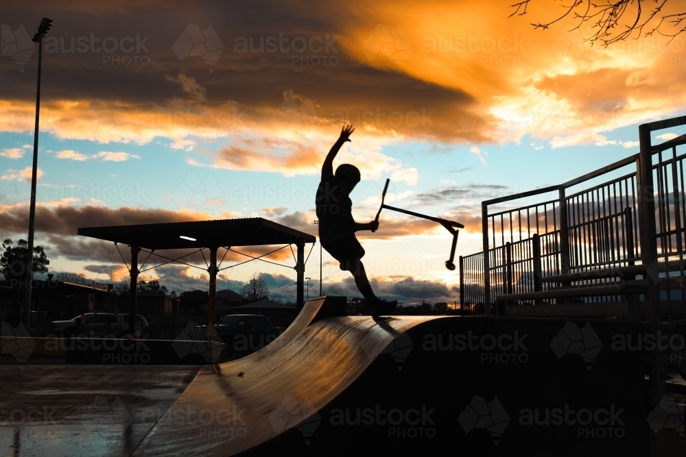 Image of Silhouette of boy riding scooter on skate park ramp at sunset ...