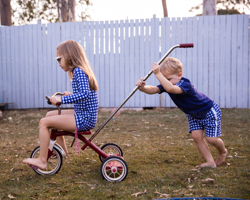 Image of sister and brother riding a trike in a back yard - Austockphoto