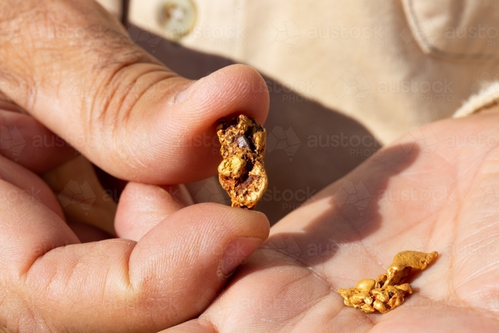Image of small gold nugget held between thumb and forefinger - Austockphoto