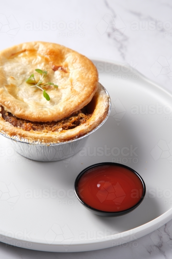 Image of Small open meat pie with side of tomato sauce - Austockphoto