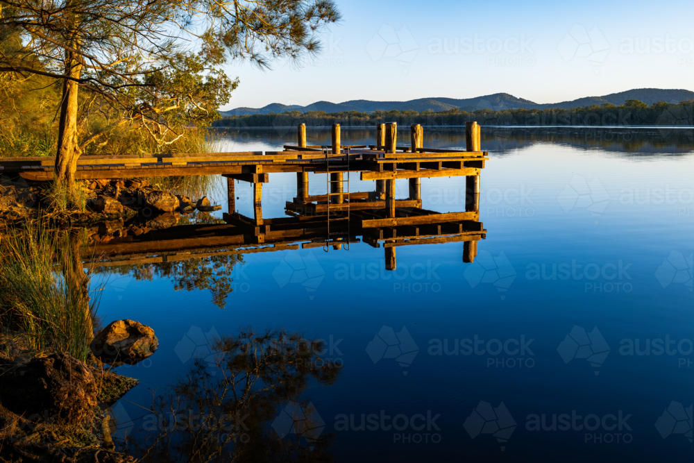 Image of Small timber jetty at sunrise beside calm water - Austockphoto