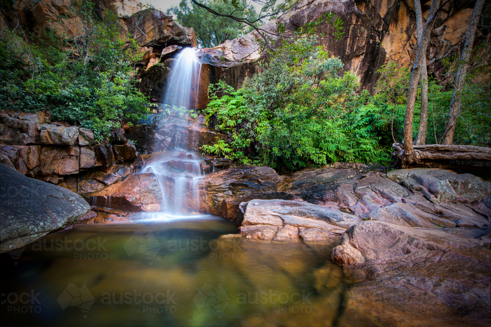 Image of Small waterfall cascading over rocky ledges into a clear pool ...