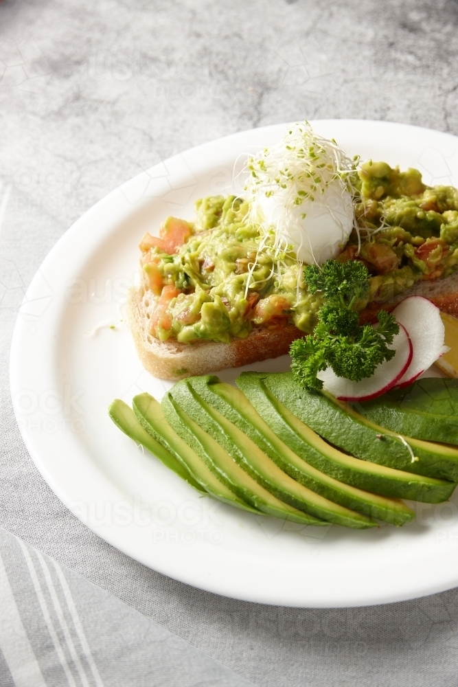 Image of smashed avo toast served on a white plate with avocado slices ...