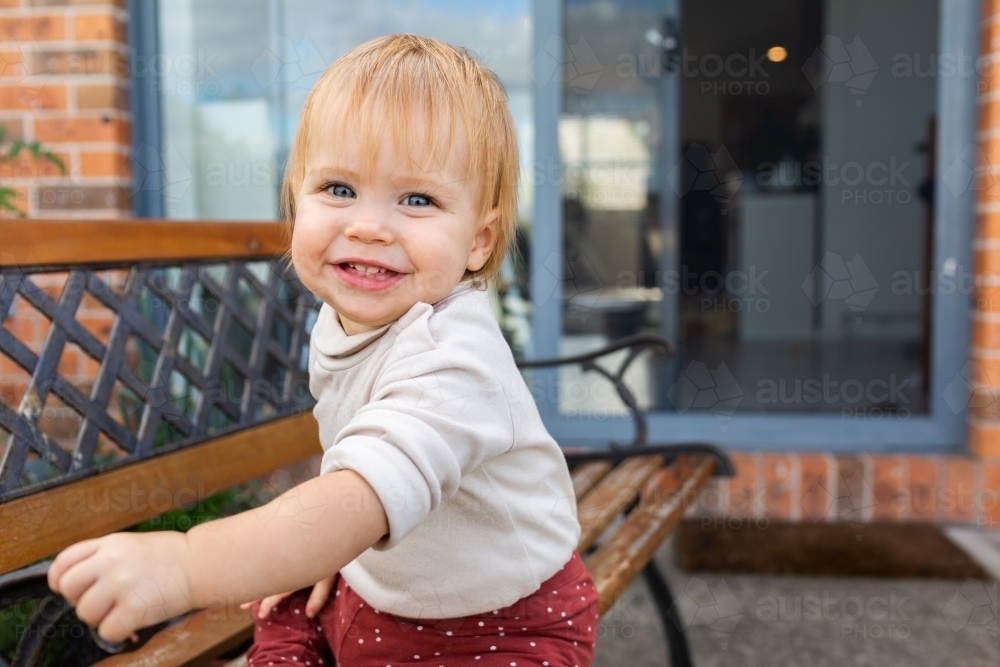 Image of Smiling baby girl sitting on park bench outside on back porch ...