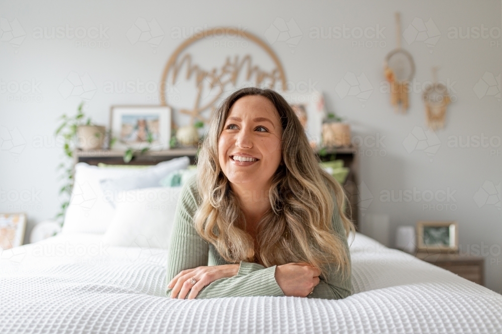 Image of Smiling blonde woman lying on the bed, looking away from ...