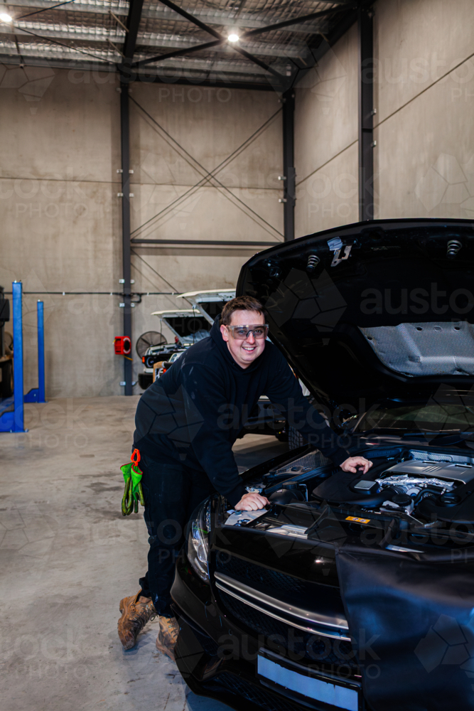 Image of Smiling male mechanic leaning over vehicle engine inside ...