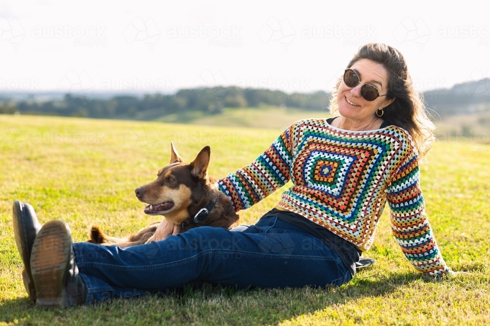 Image of Smiling middle age Aussie woman sitting on farm lawn with pet ...