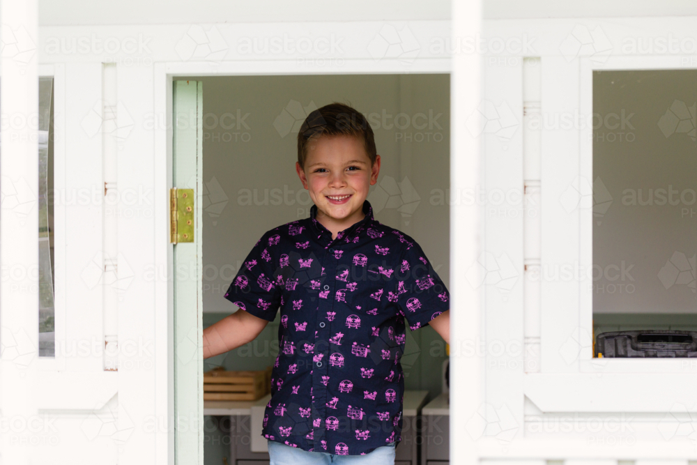 Image of Smiling young boy playing alone in cubby house doorway ...