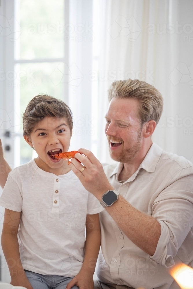 Image of Son eating prawn out of dad's hand - Austockphoto