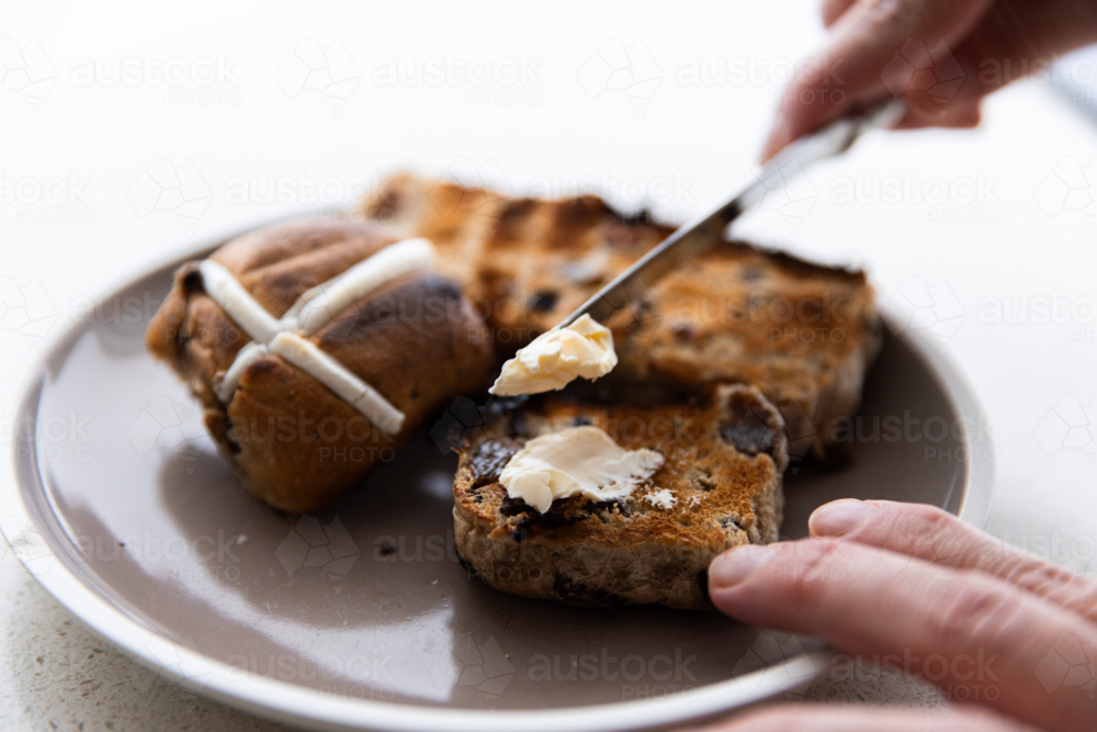 Image of spreading butter onto a toasted hot cross bun - Austockphoto