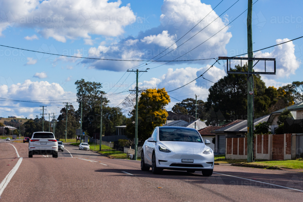 Image of Streetscape of cars passing on road with EV car - Austockphoto