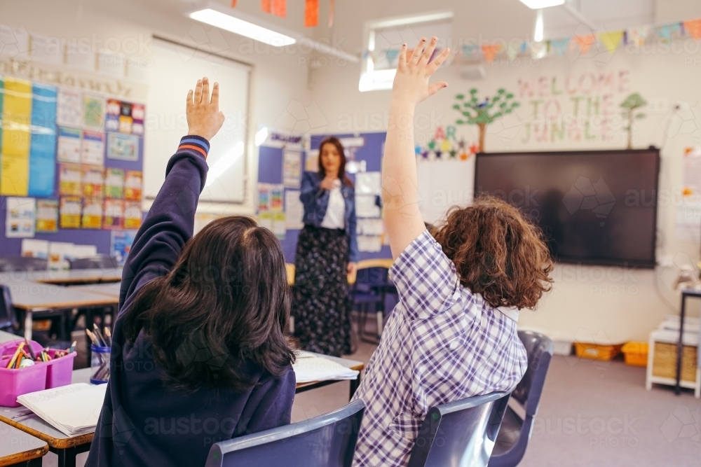 Image of Students in a classroom with their hands up - Austockphoto