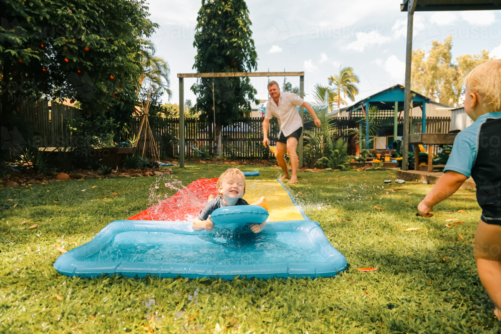 Image of Summer backyard slip and slide family fun - Austockphoto