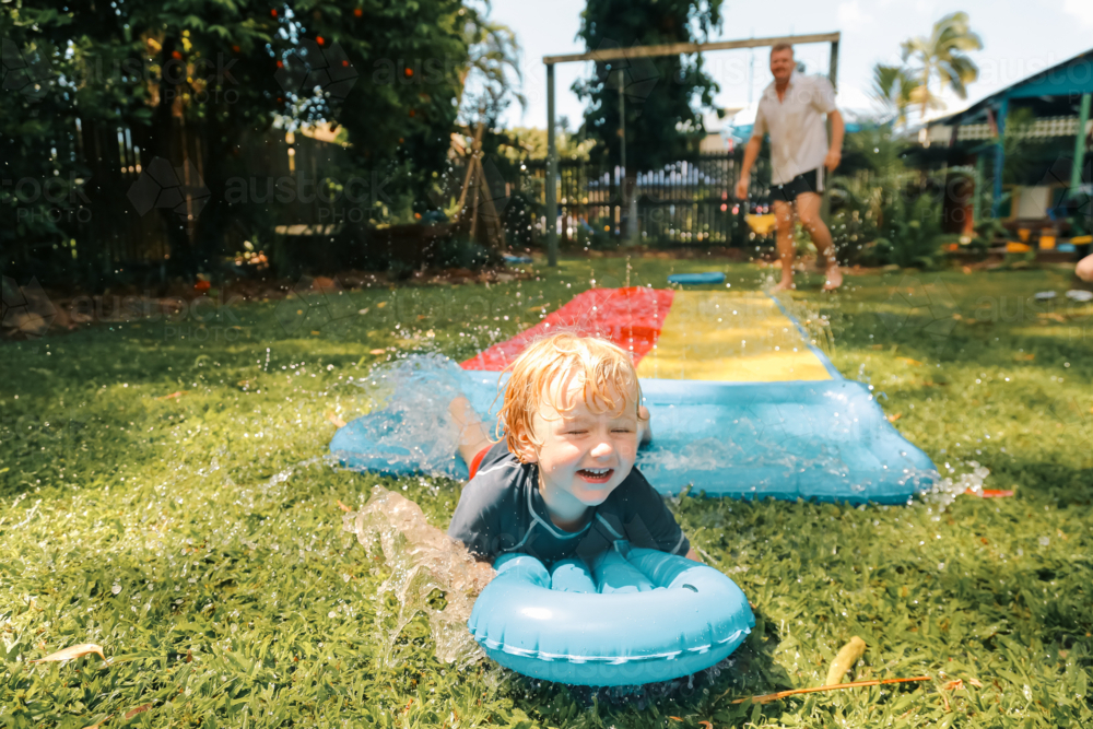 Image of Summer backyard slip and slide family fun - Austockphoto