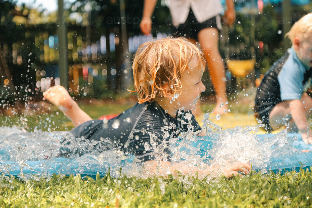 Image of Summer backyard slip and slide family fun - Austockphoto