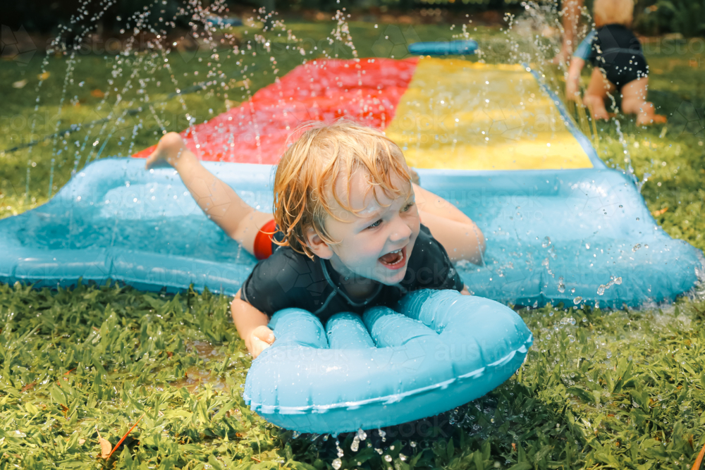 Image of Summer backyard slip and slide family fun - Austockphoto