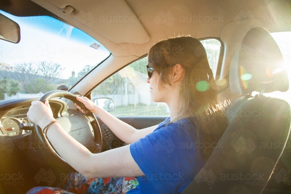 Image of Sun flare over learner driver driving car through town ...