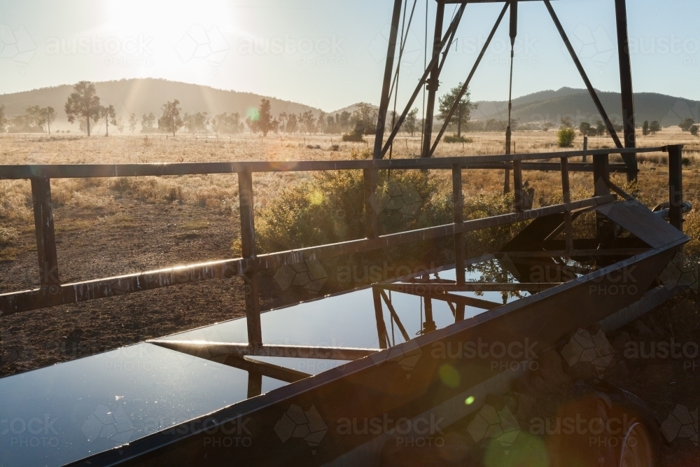 Image of Sun flare over water trough on farm with windmill - Austockphoto