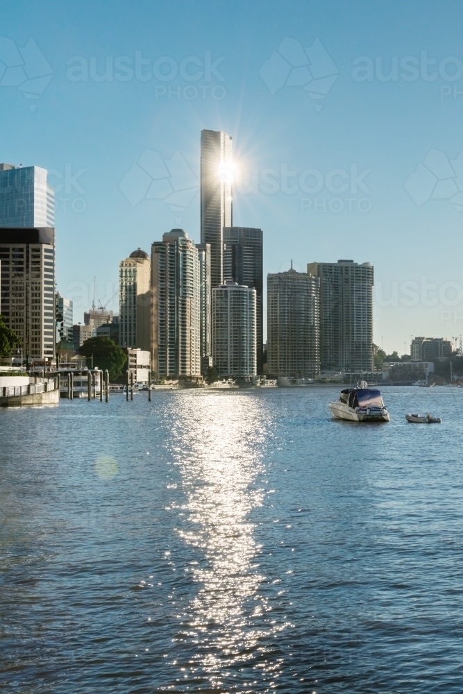 Image of sun reflecting off tall city building over water - Austockphoto