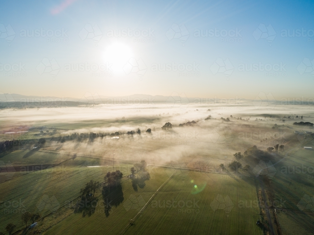 Image of Sun rising in sky with aerial view over misty landscape of ...