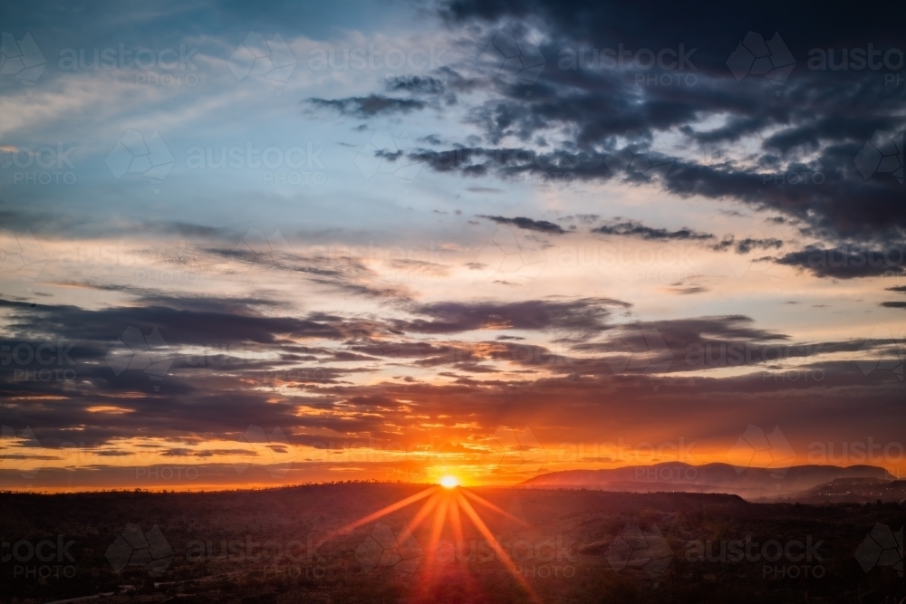Image of Sun setting in cloudy sky over rural landscape - Austockphoto