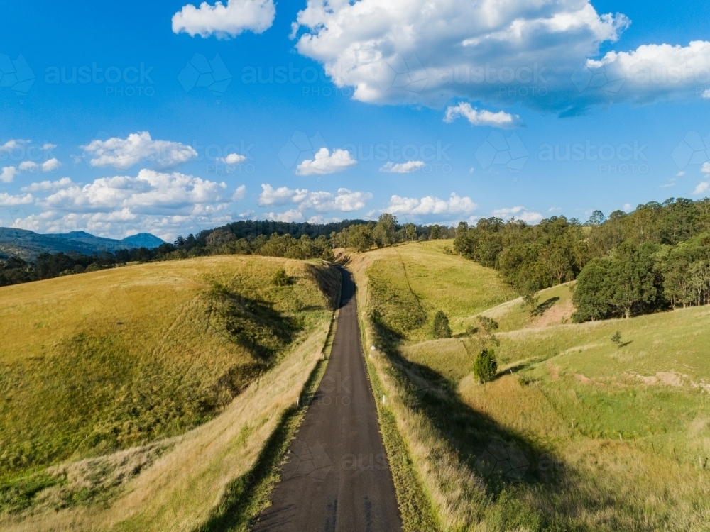 Image of Sunlit country road in rural paddock landscape - Austockphoto