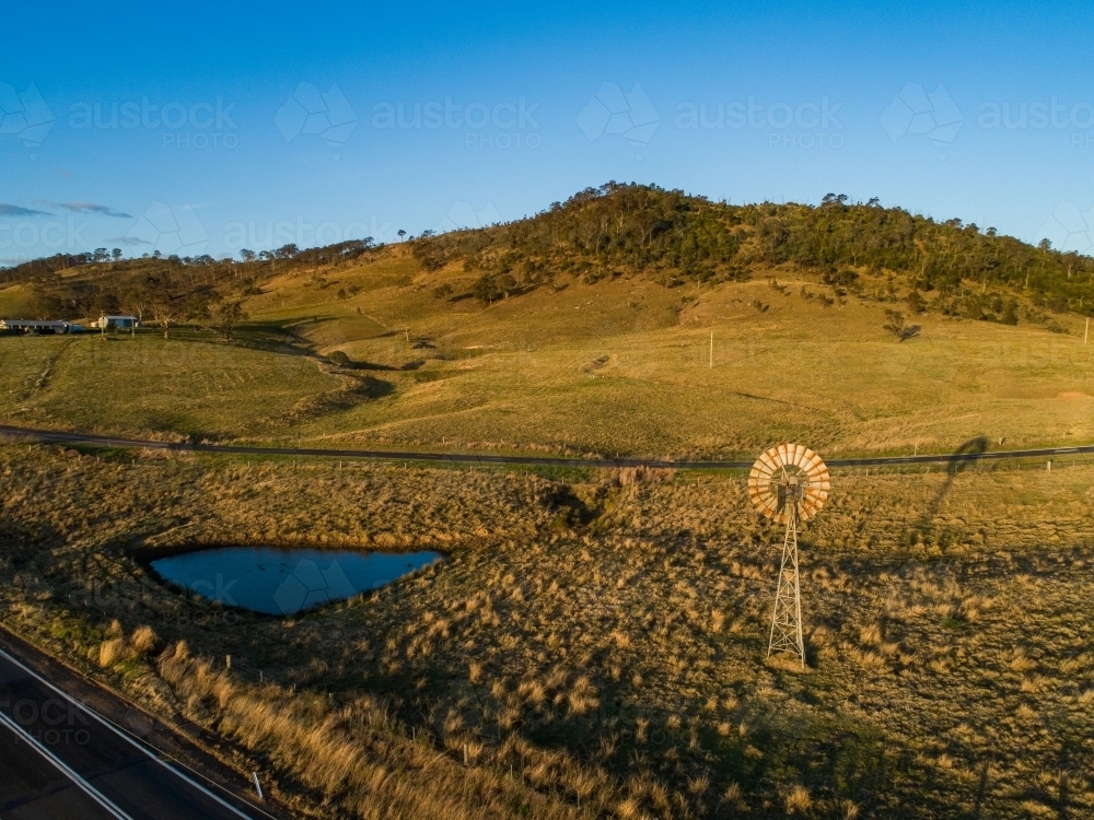 Image of Sunlit farm paddock with small dam and windmill beside country ...