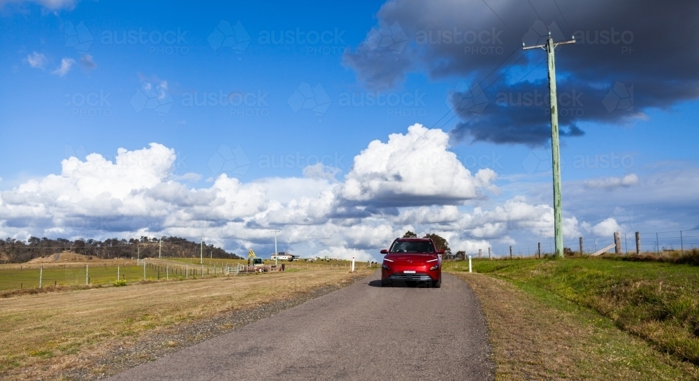 Image of Sunlit red environmentally friendly ev car driving down remote ...