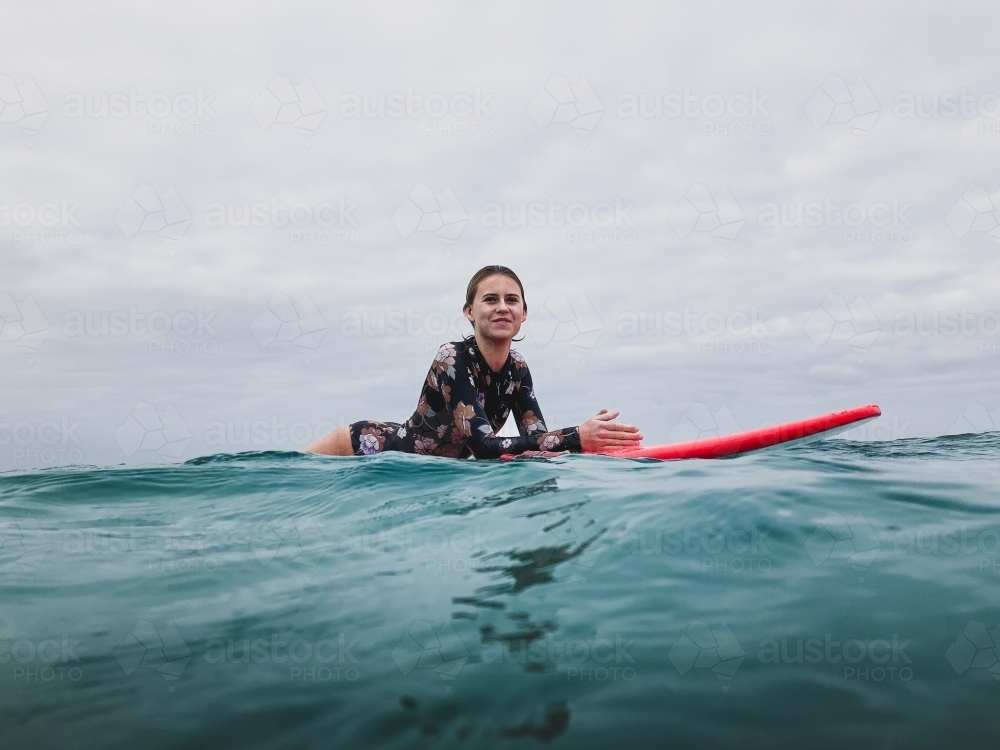 Image of Surfing Teenage girl lying on red surfboard in ocean wearing ...