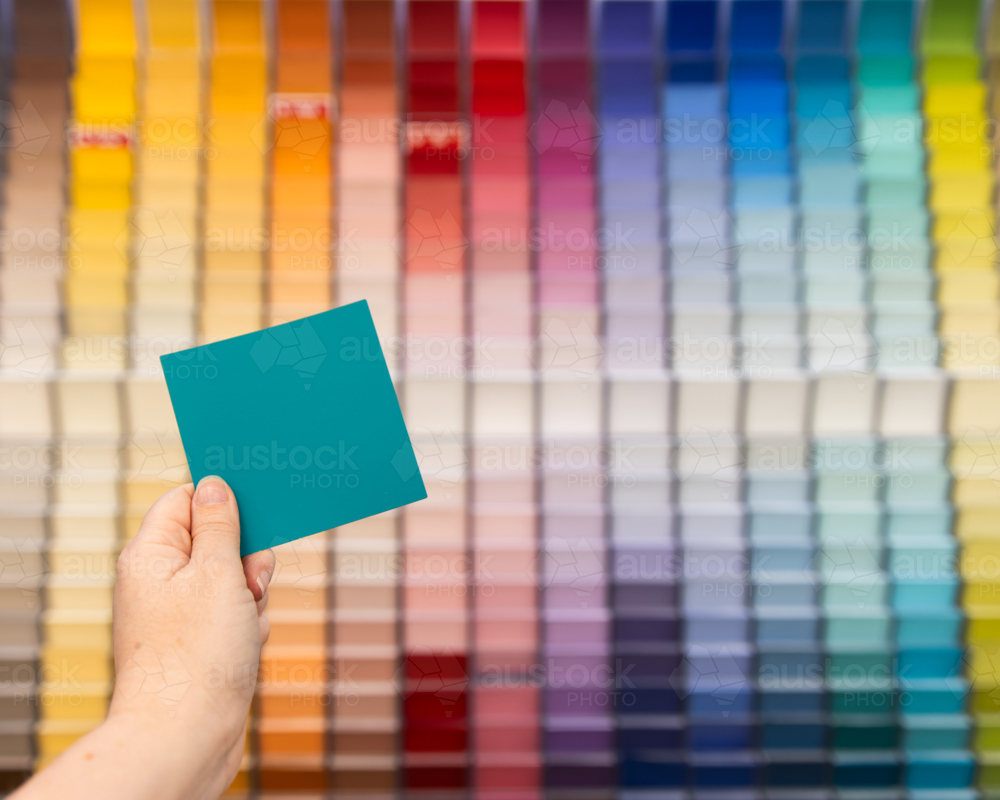 Image of teal paint colour card held up in front of paint sample wall ...
