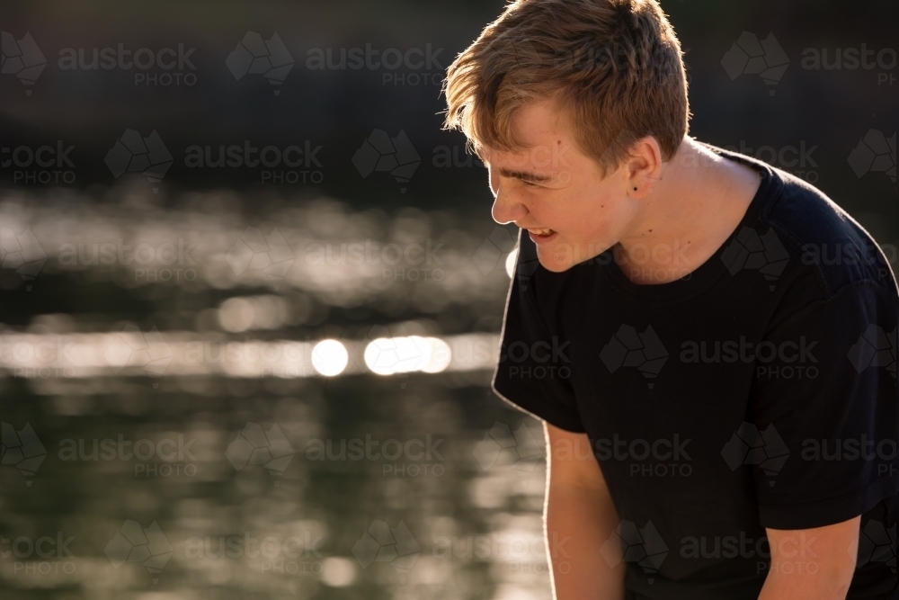 Image of Teen boy laughing at water's edge in golden afternoon light ...