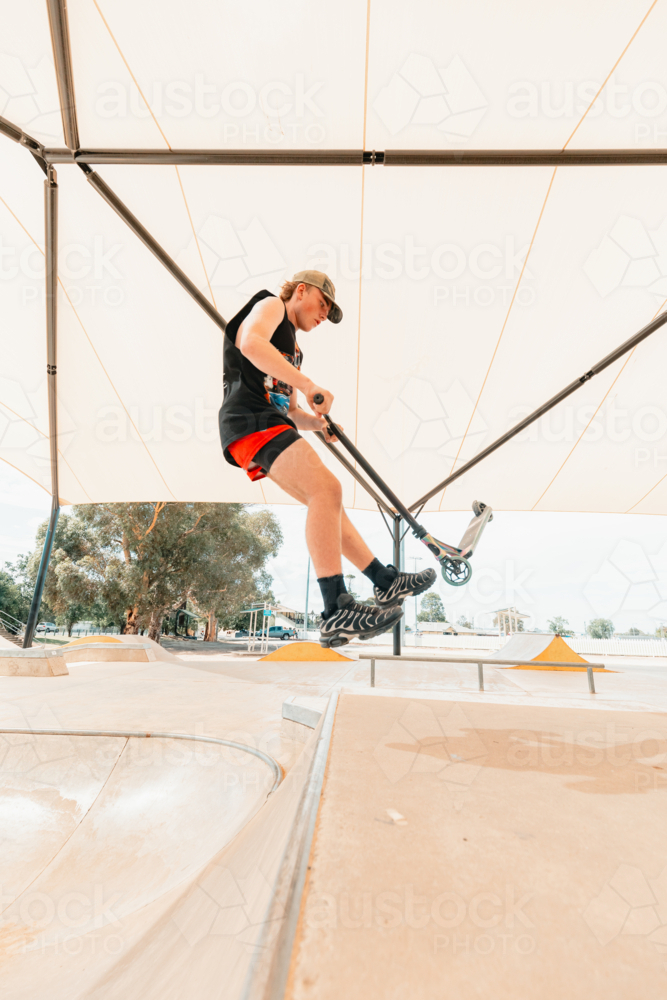 Image of Teen boy riding scooter on ramps at skate park - Austockphoto