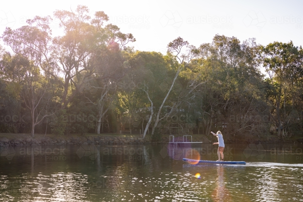 Image of Teen boy riding stand up paddle board in golden afternoon ...