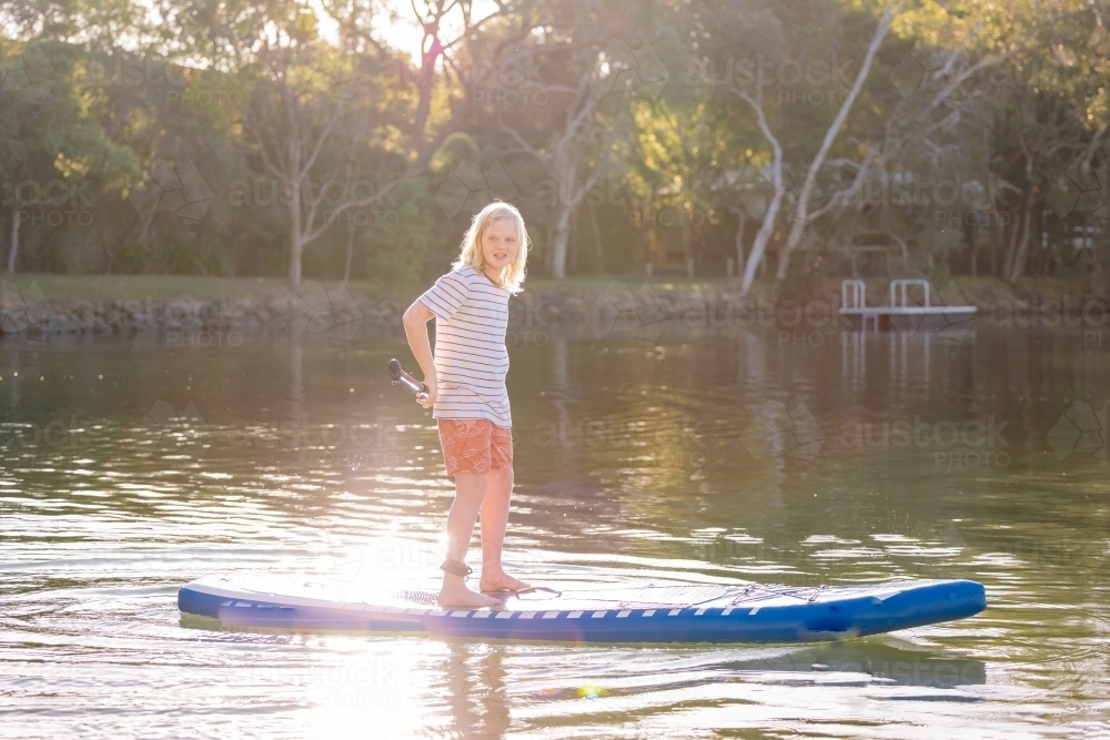 Image of Teen boy riding stand up paddle board in golden afternoon ...